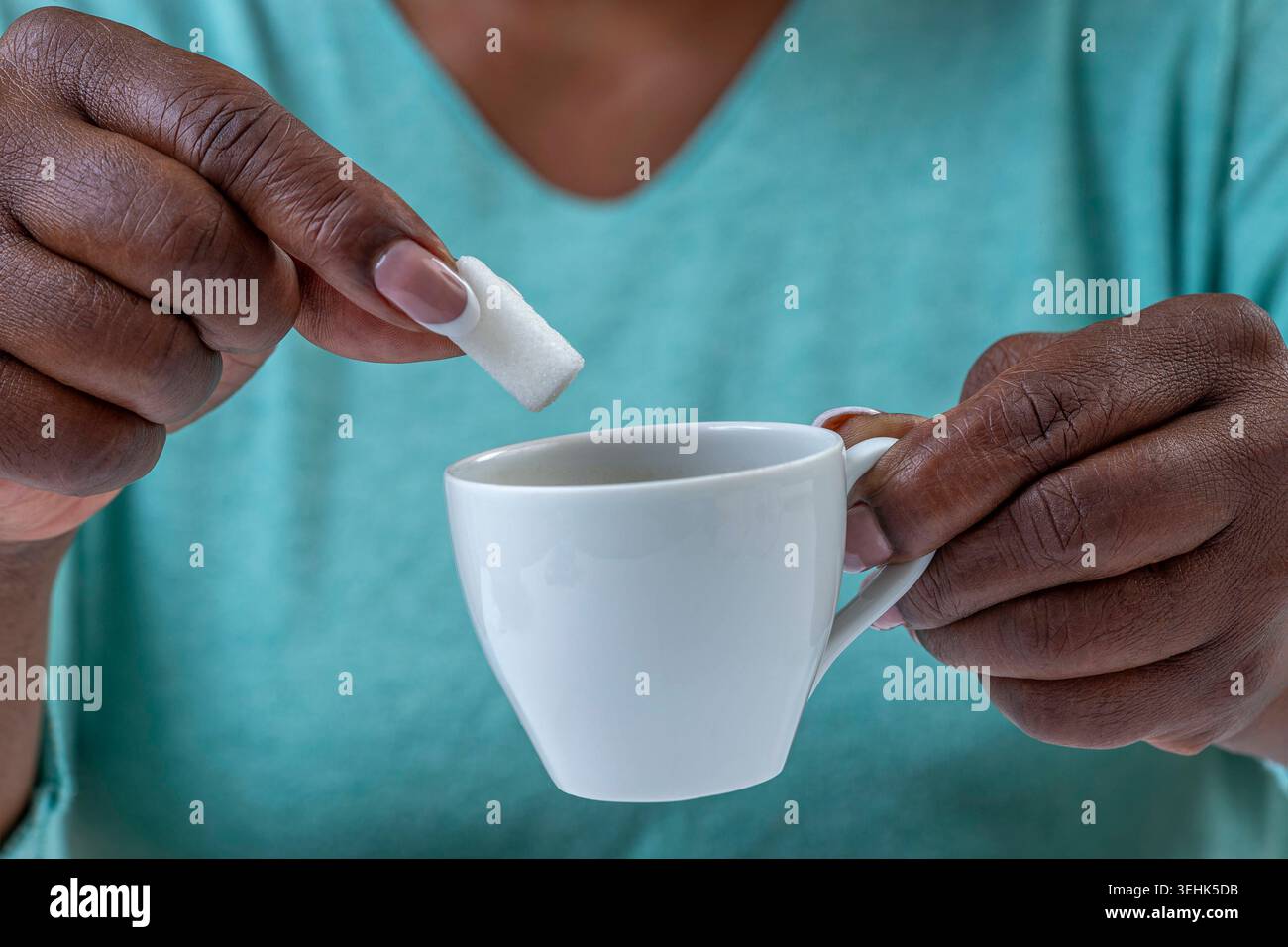 A person holds a white ceramic cup in one hand and a sucrose cube in ...