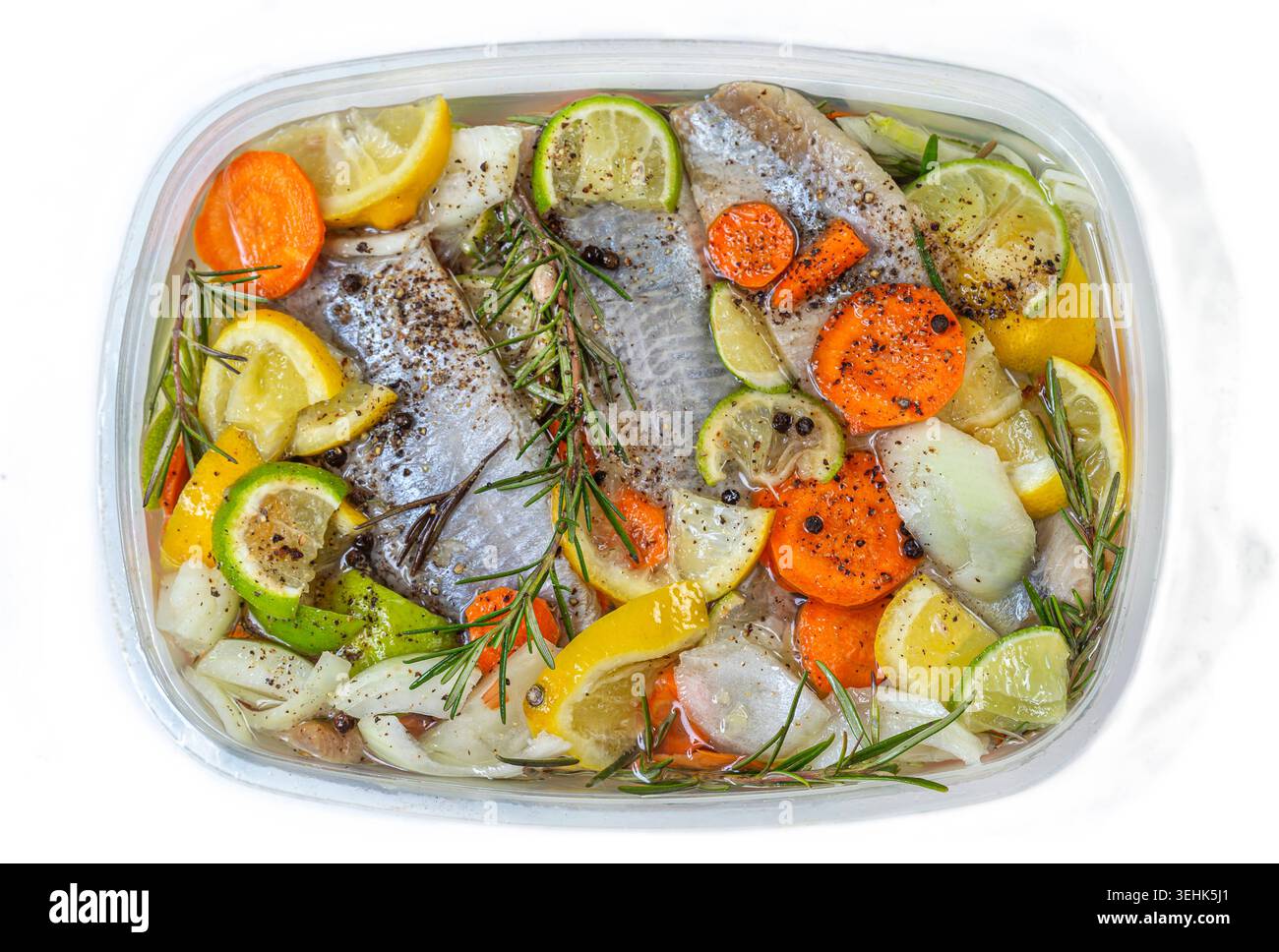 Raw fish fillets are in a glass dish with lemon and lime slices, carrot ...