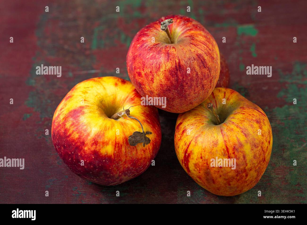 Three apples Malus domestica with red and yellow skin are stacked on a ...