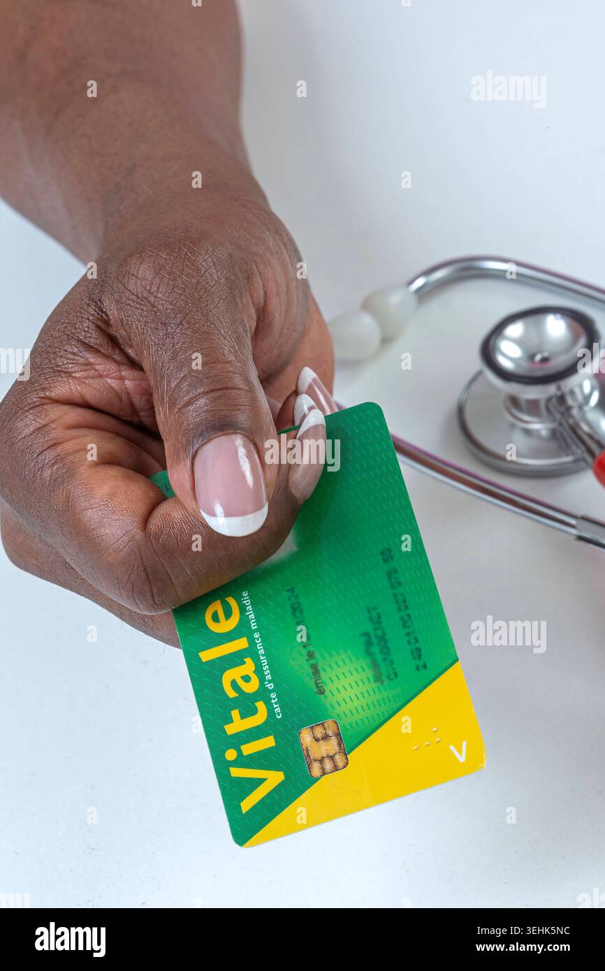 A human hand holds a green and yellow health insurance card. A ...