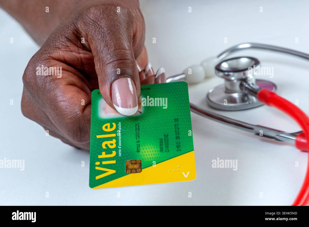 A hand holds a Carte Vitale next to a stethoscope on a white surface ...