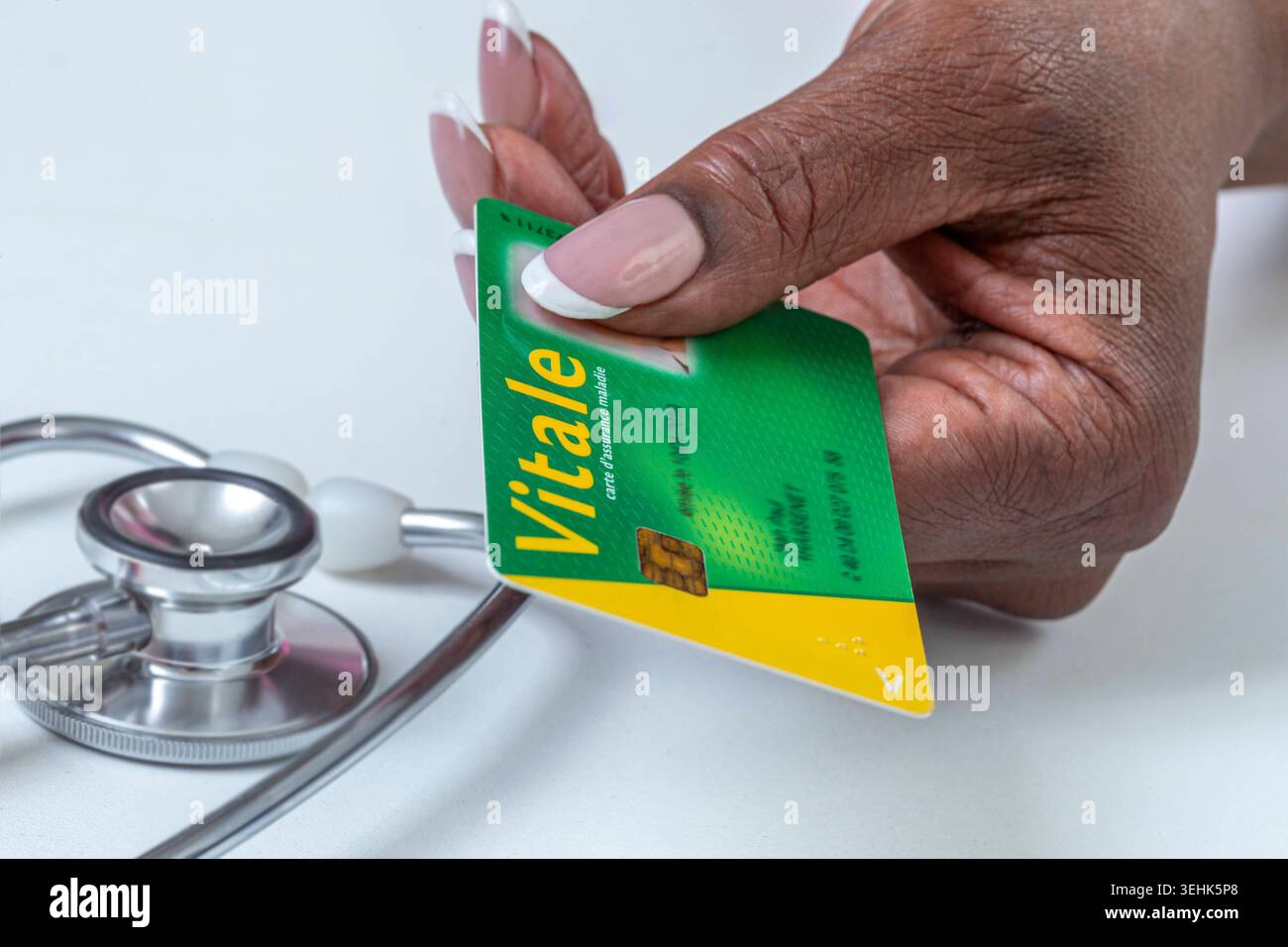 A hand holds a Carte Vitale next to a stethoscope on a white surface ...