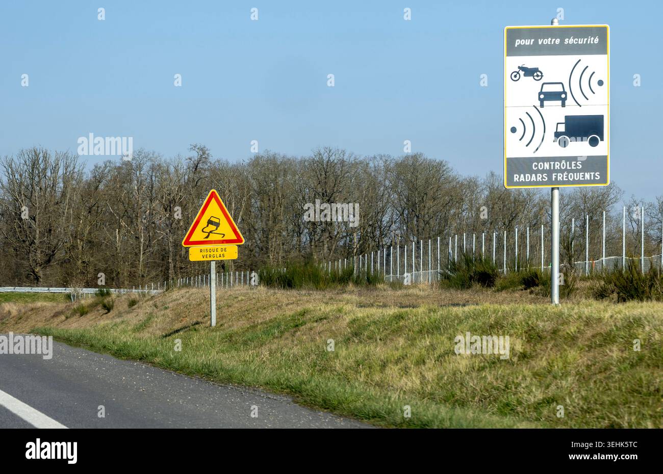 Two road signs stand on a grassy verge next to a paved road, with a ...