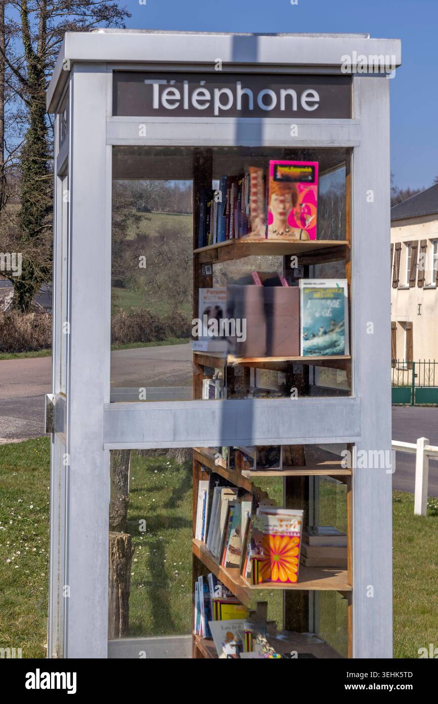 A white telephone booth contains wooden shelves filled with books. It ...