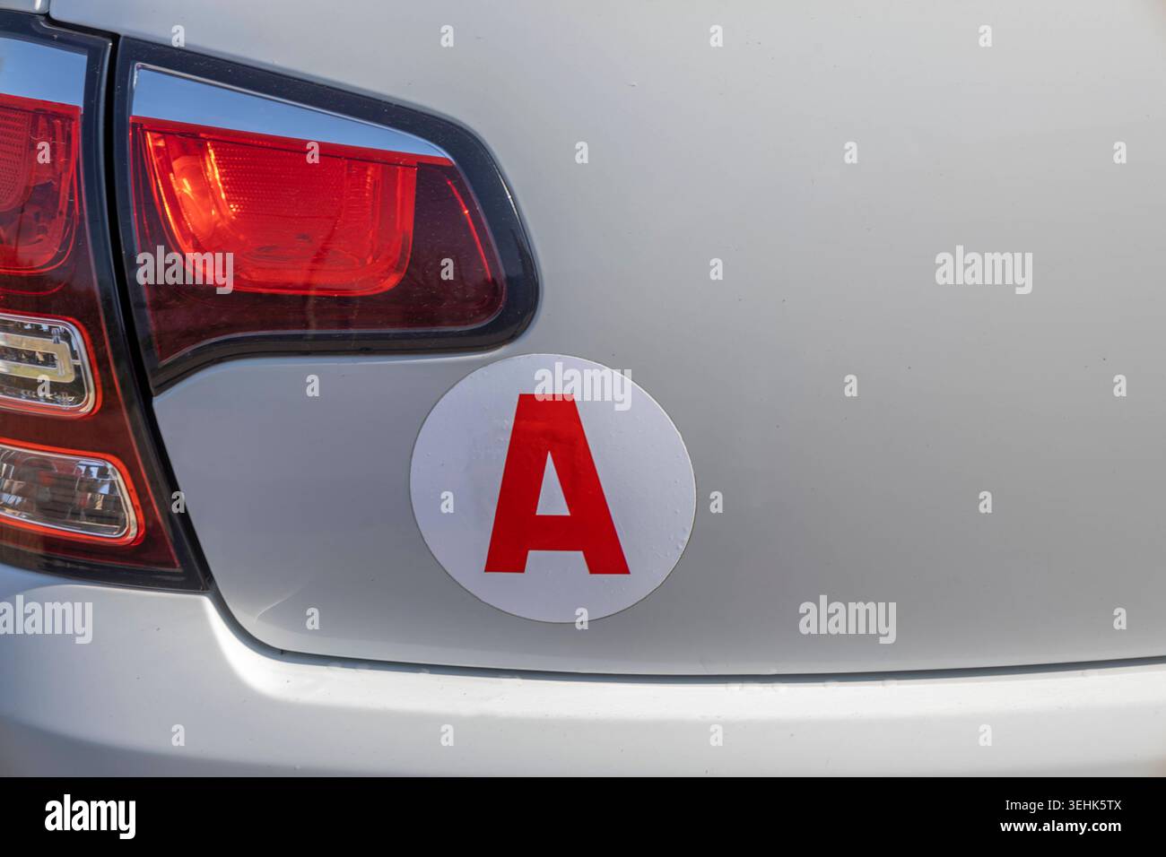 A close-up shows the rear of a white car. A red taillight is visible ...
