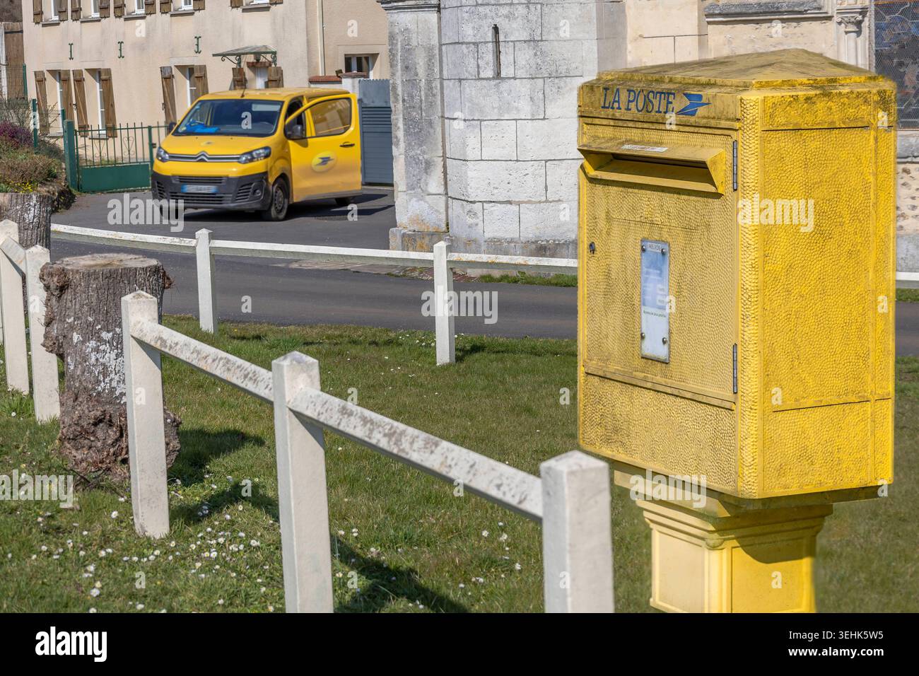 A yellow mailbox stands on a grassy area next to a white fence. In the ...