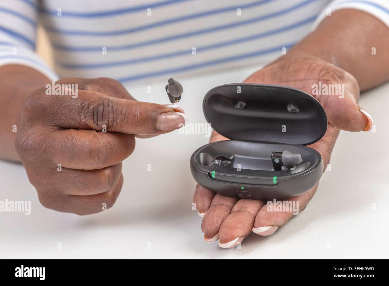 A person holds a pair of wireless earbuds and their charging case. One ...