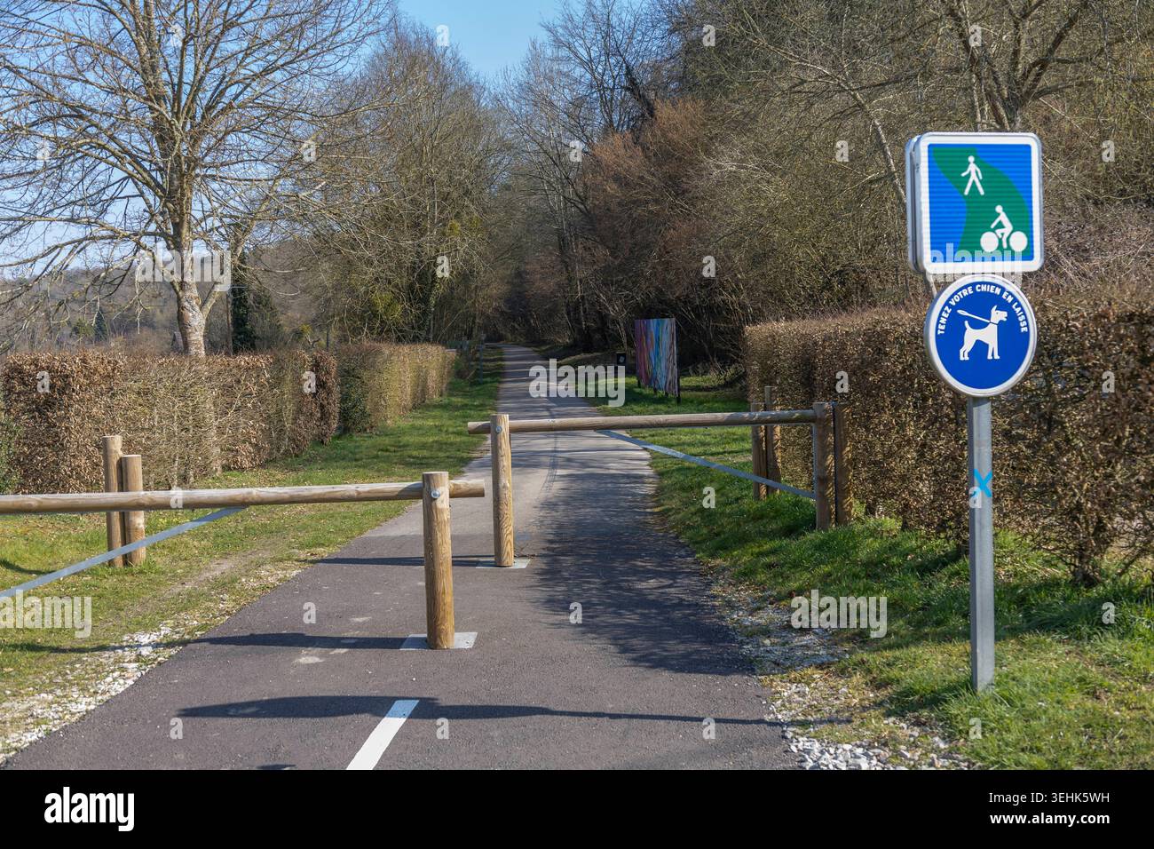 A paved path leads through a wooded area. Wooden barriers cross the ...