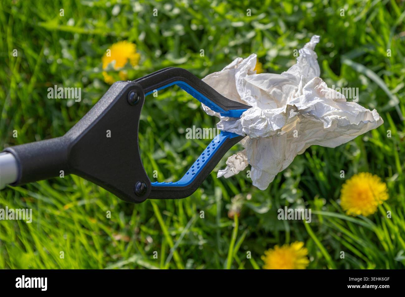 A litter picker tool grips a piece of crumpled white paper over a green ...