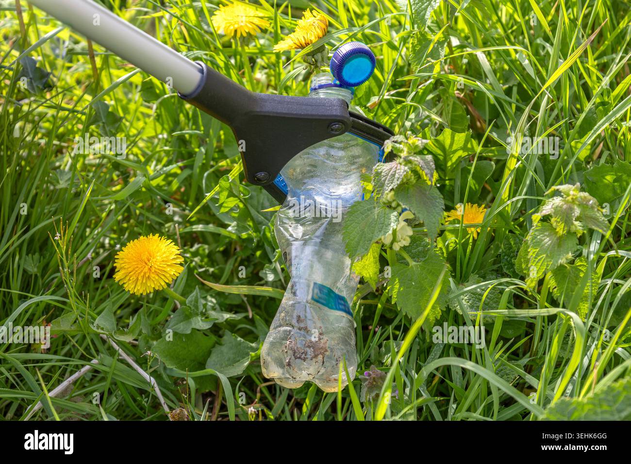 A litter picker tool grips a clear plastic bottle with a blue cap in a ...