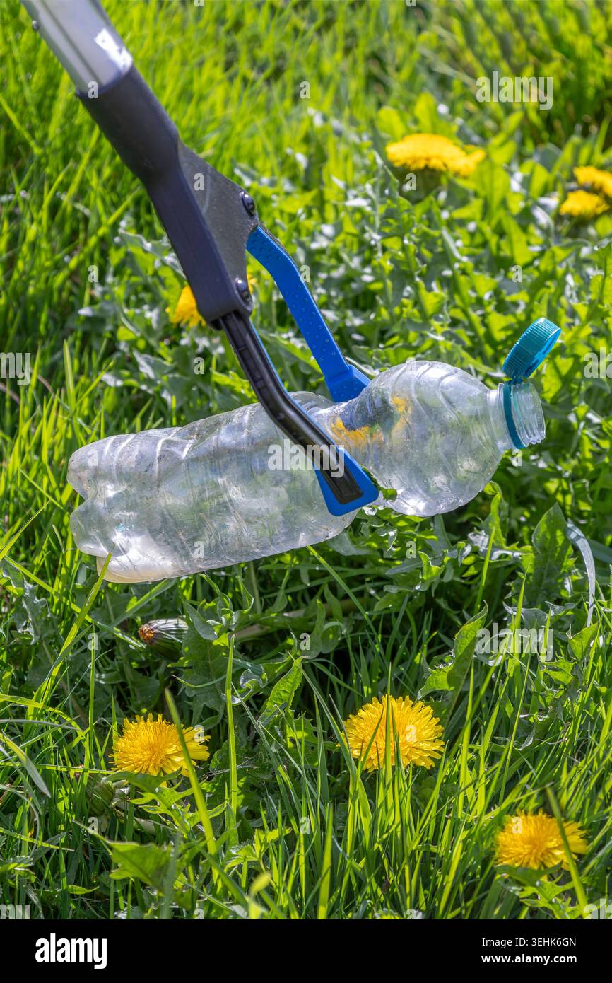 A mechanical grabber tool picks up a clear plastic bottle from a grassy ...