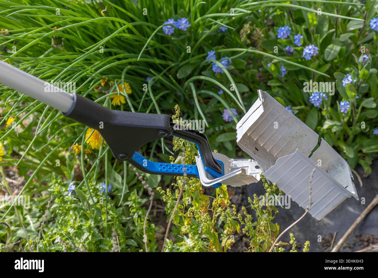A mechanical reacher tool with a blue grip picks up a piece of metal ...