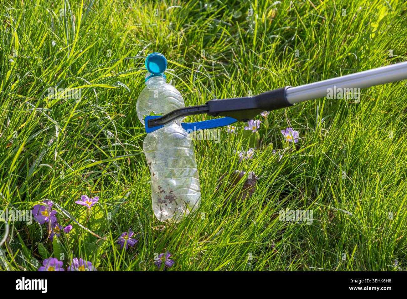A litter picker tool grips a clear plastic bottle with a blue cap in a ...
