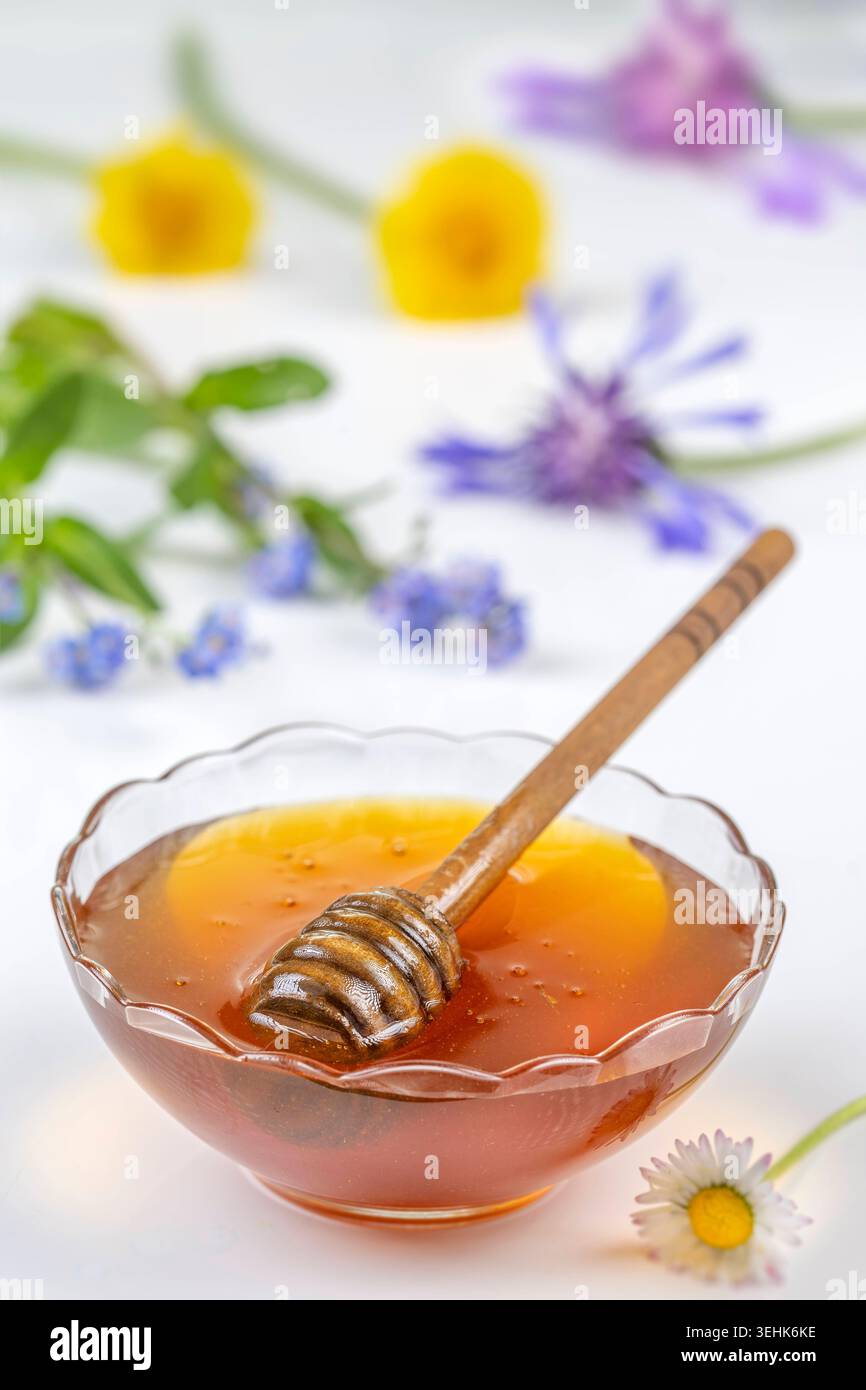 A glass bowl contains a viscous amber liquid and a wooden honey dipper ...