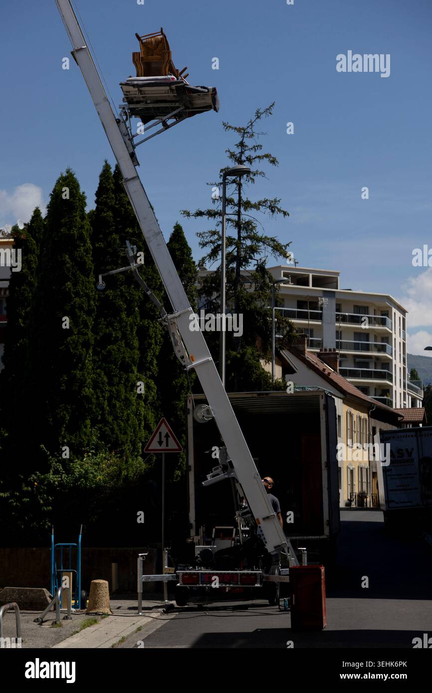 Movers use a furniture lift to lower a piece of furniture from an ...
