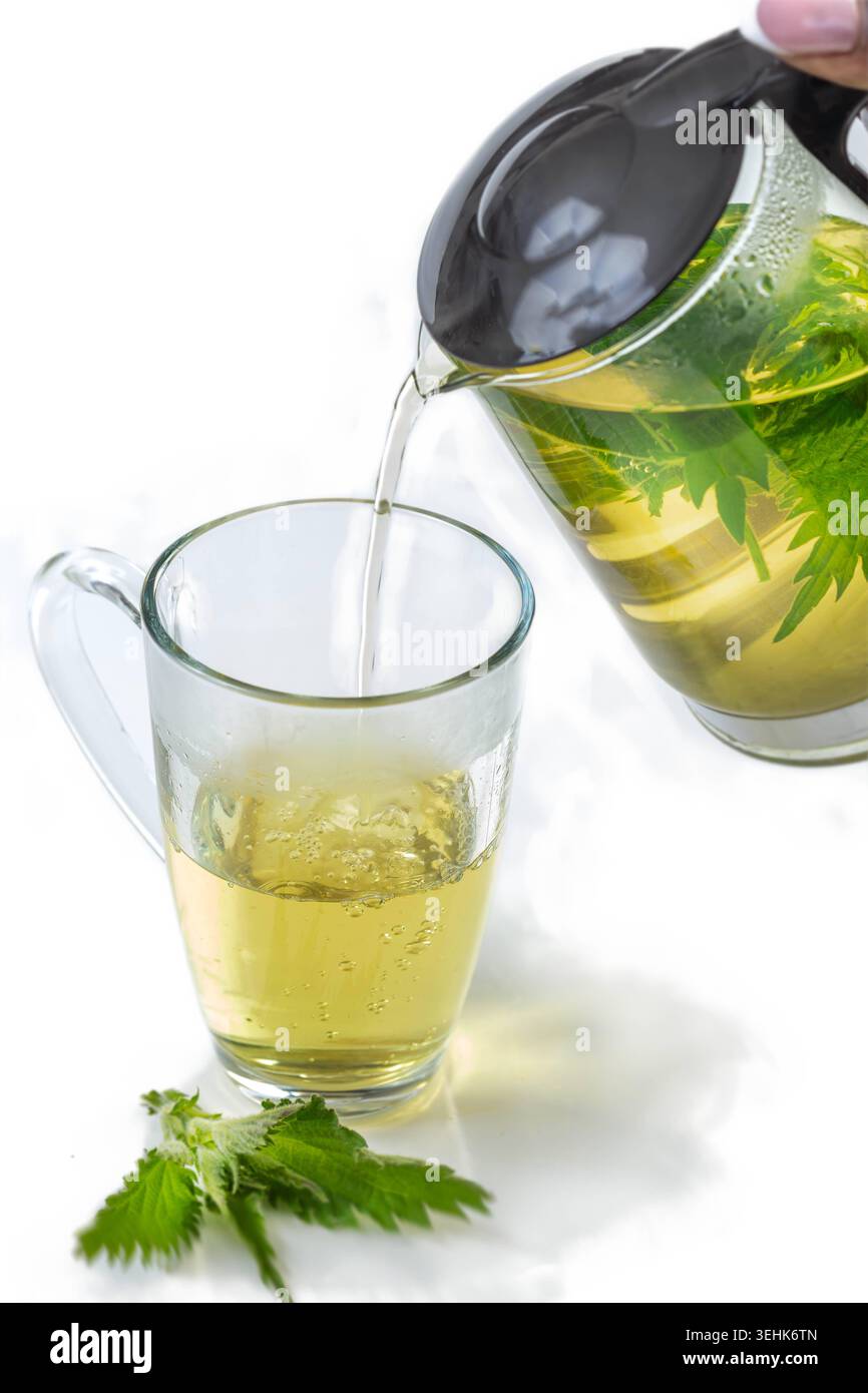 A yellow liquid is poured from a glass teapot containing green leaves ...