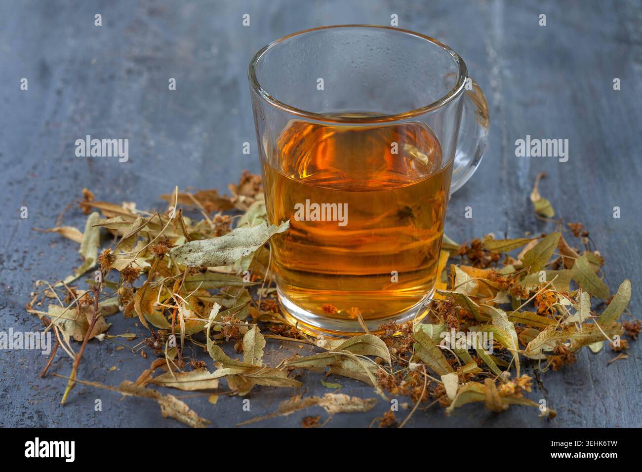 A glass mug containing an amber liquid sits on a dark surface ...