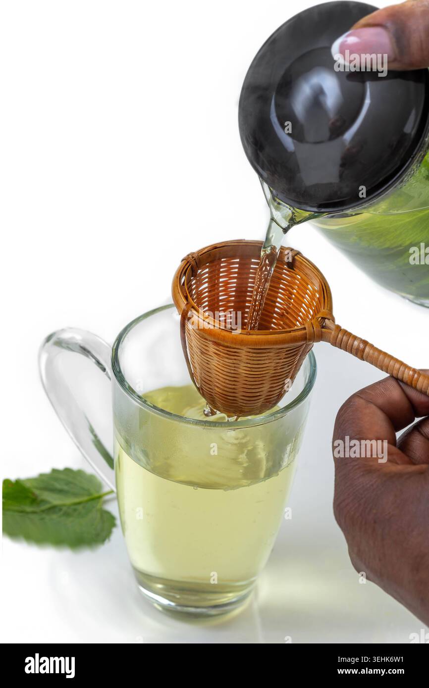 A person pours a yellow liquid from a teapot through a woven strainer ...