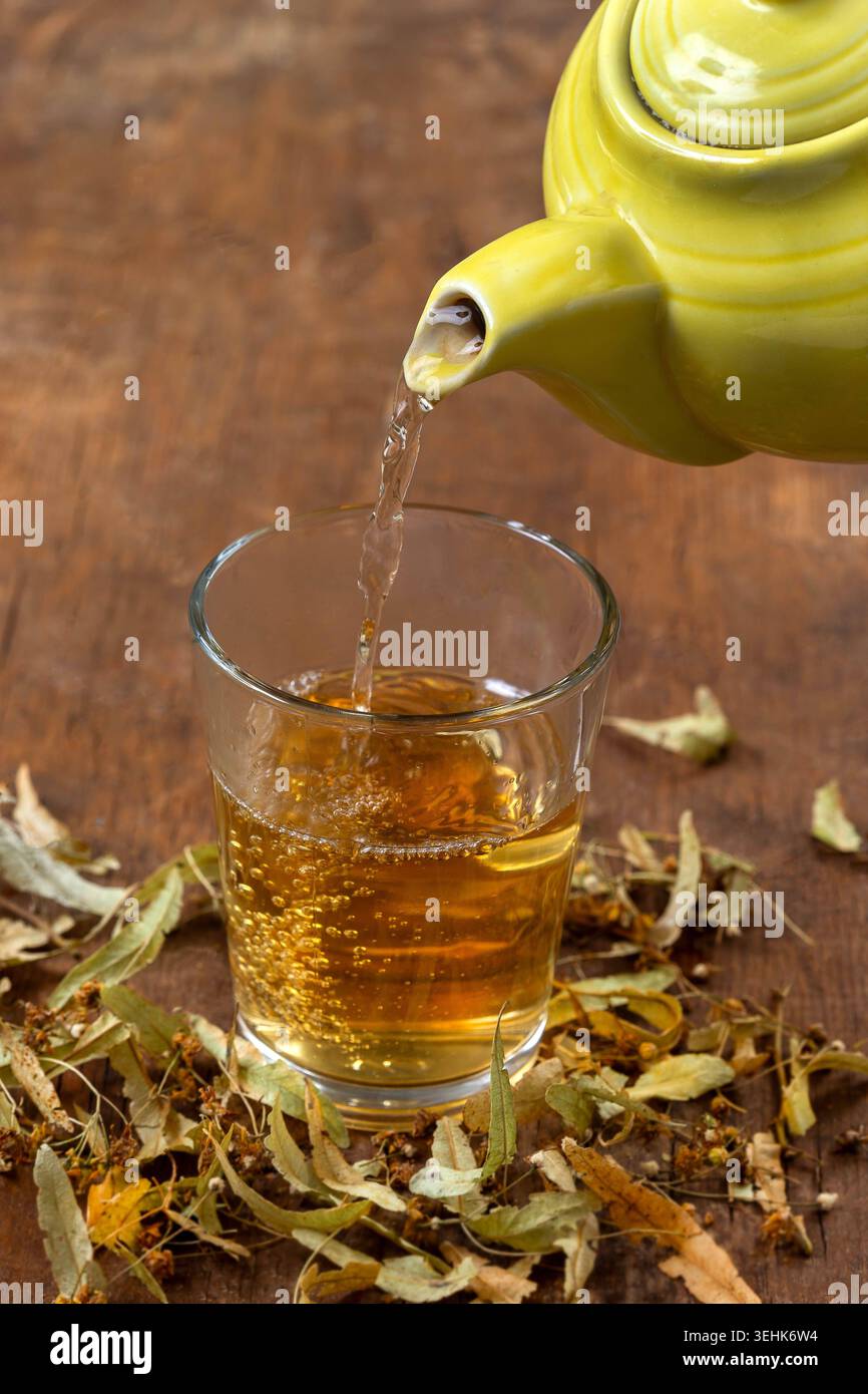A yellow teapot pours a golden liquid into a glass. Dried leaves and ...
