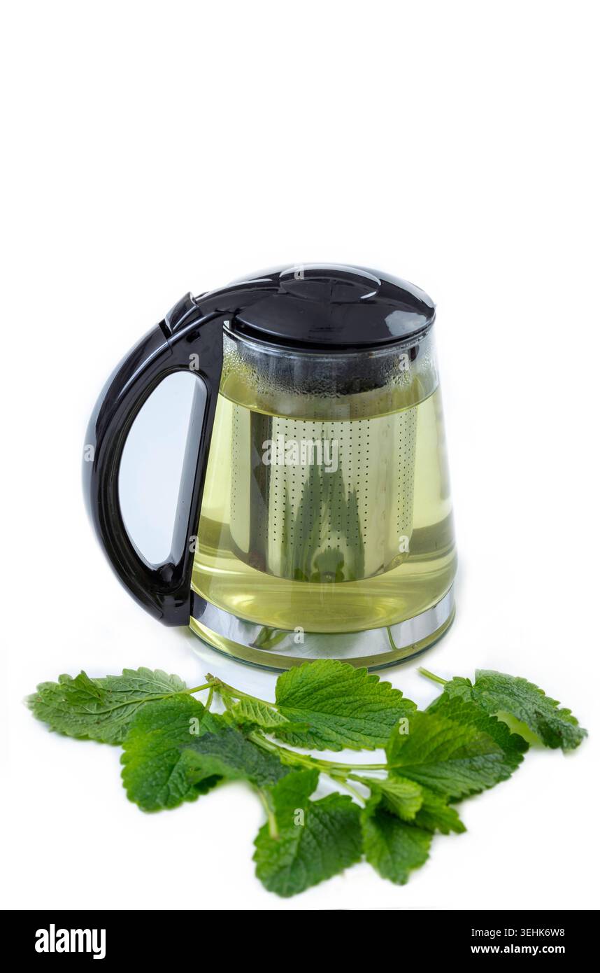 A glass mug with a black handle and lid contains a yellow liquid and a ...