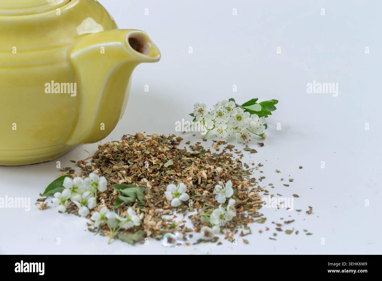 A yellow teapot sits next to a pile of dried herbs and fresh hawthorn ...