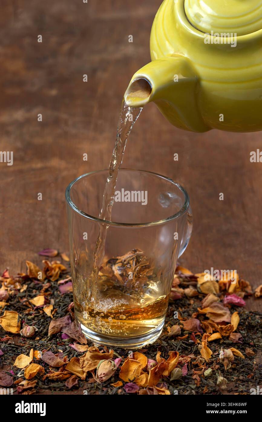 A yellow teapot pours a golden liquid into a glass cup. The cup sits on ...