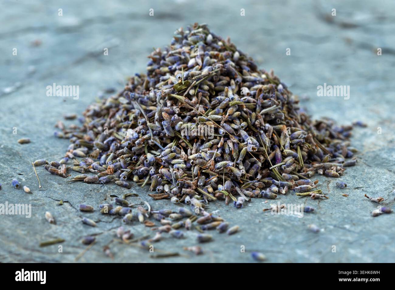 A pile of dried lavender Lavandula flower buds rests on a grey stone ...