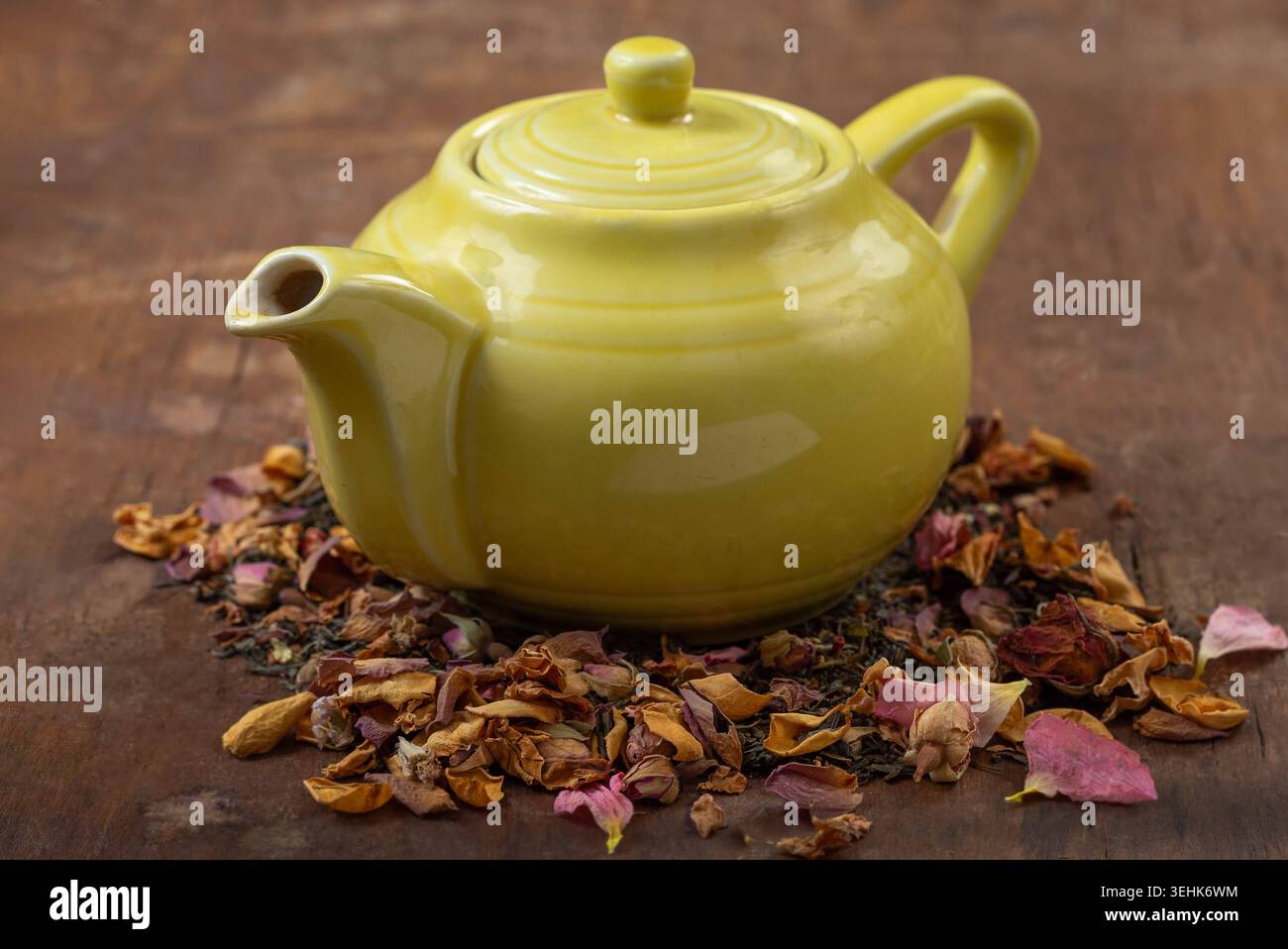 A yellow teapot sits on a wooden surface, surrounded by dried flower ...