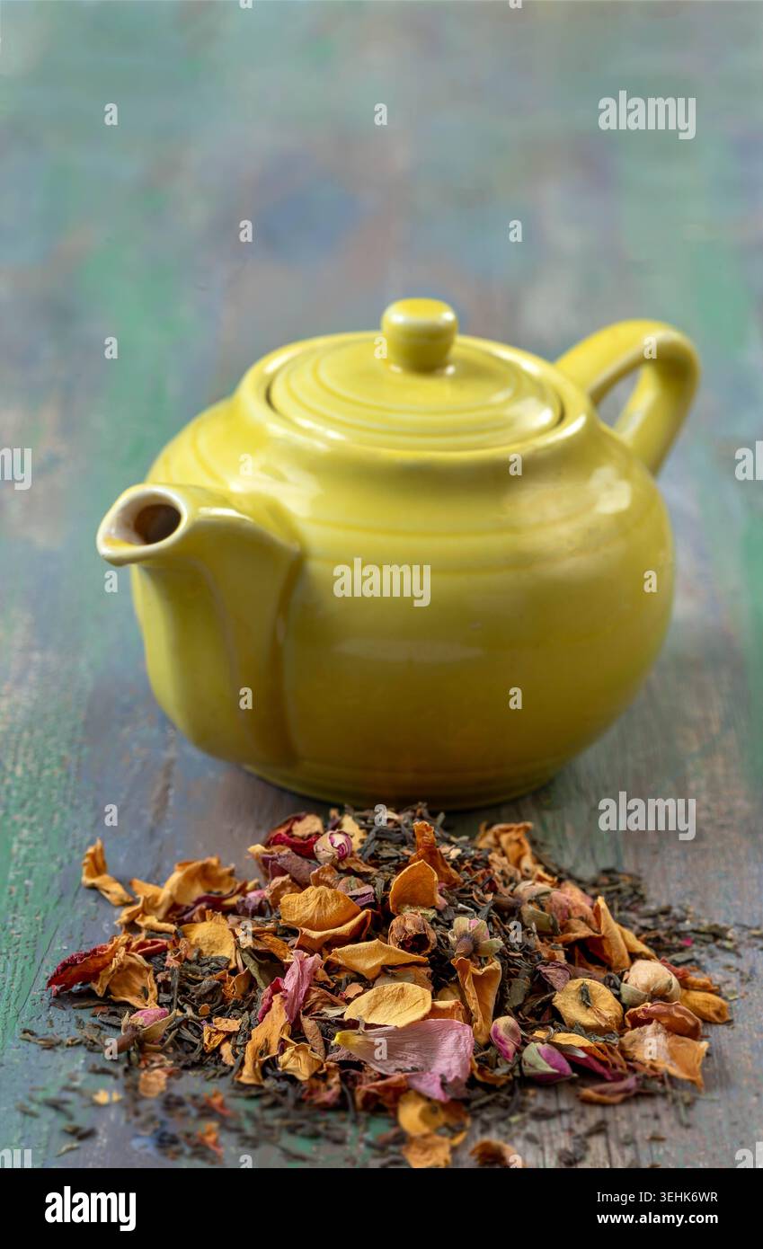A yellow teapot sits on a blue wooden surface. A pile of dried tea ...