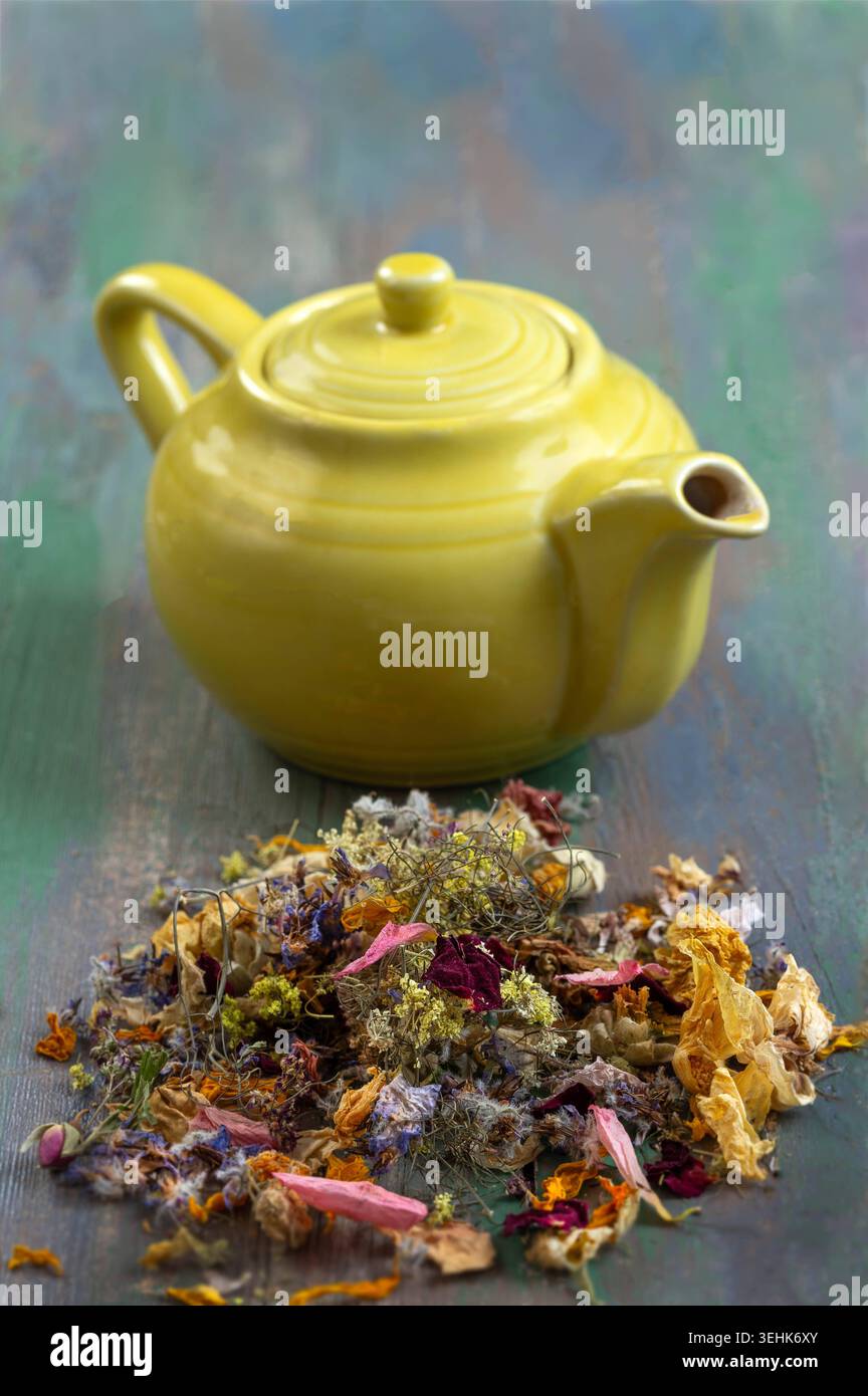 A yellow teapot sits on a blue and green wooden surface. A pile of ...