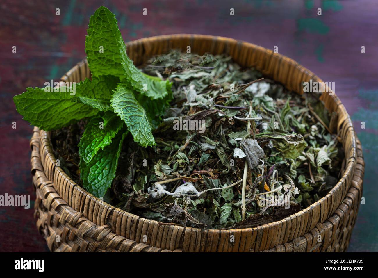 A woven basket contains dried leaves and a fresh sprig of mint Mentha ...
