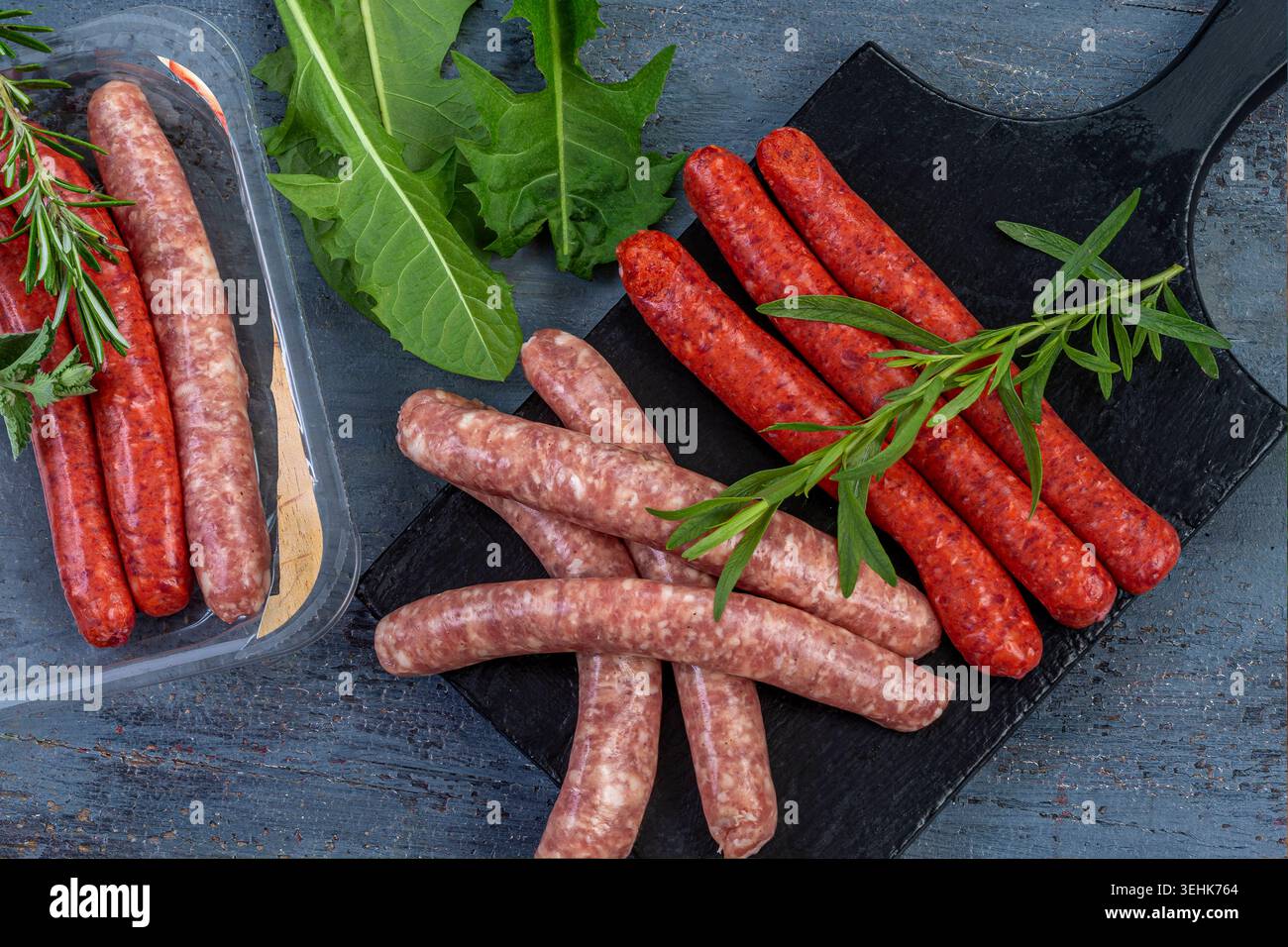 Raw red and pale sausages are arranged on a black board and in a ...