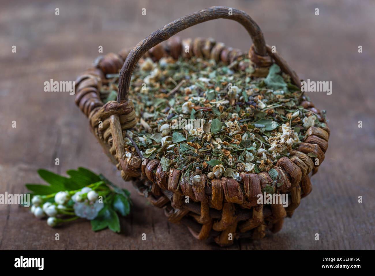 A woven basket contains a mixture of dried leaves and flowers. A sprig ...