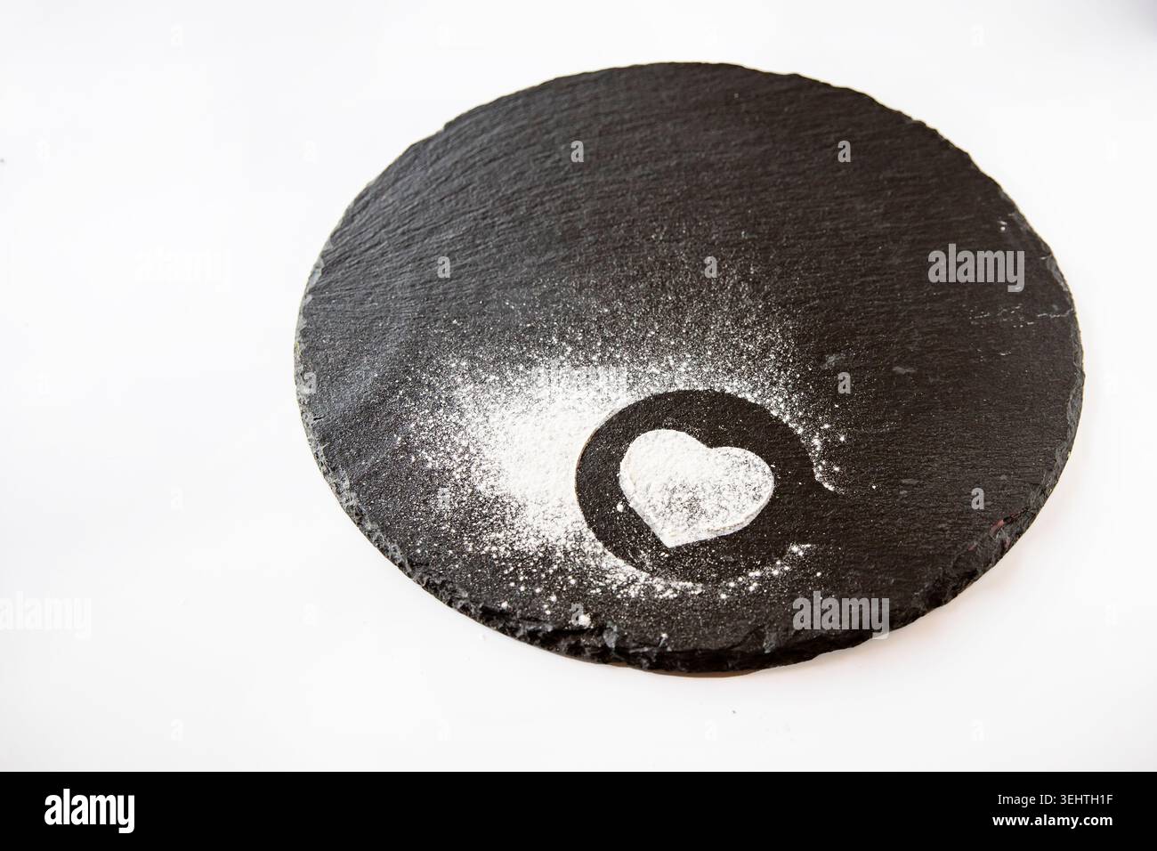 White heart shape made from flour on black round slate board with ...