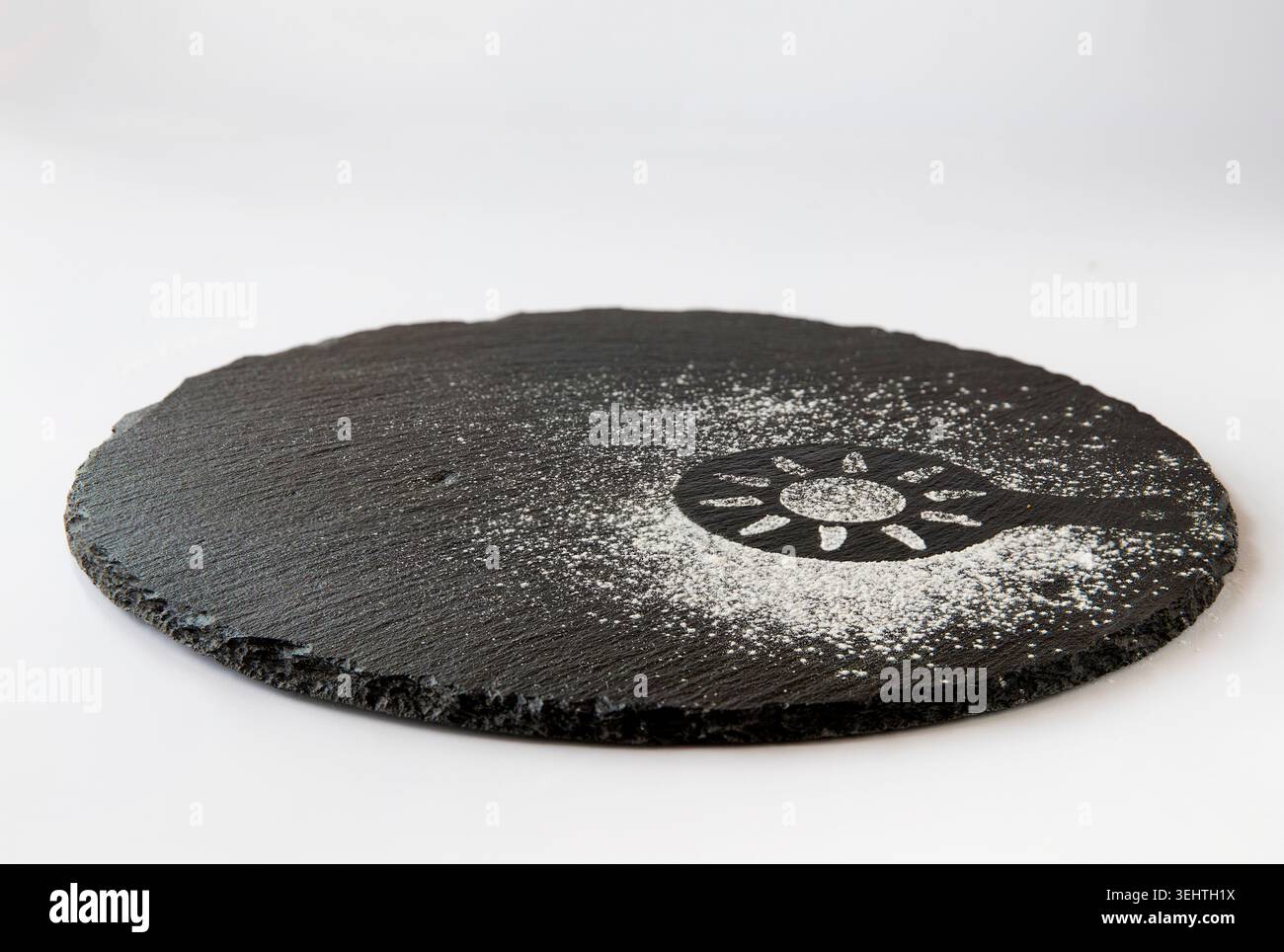 White sun symbol made from flour on black slate serving board with ...