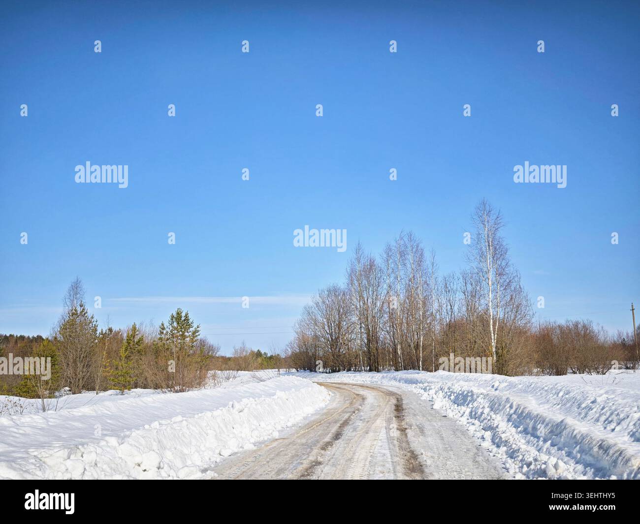 Road winds through open land with melting snow as winter transitions to ...