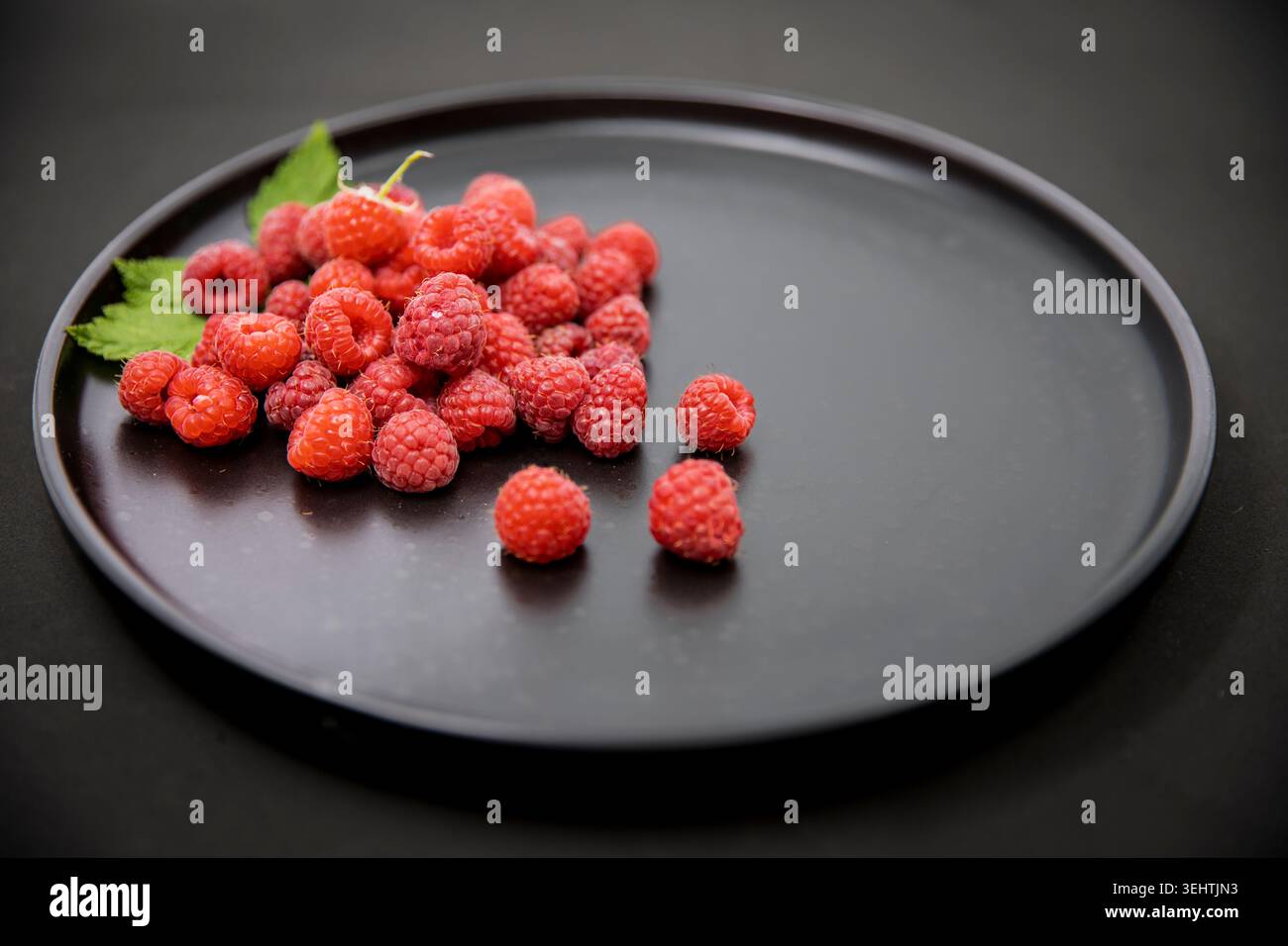 Fresh ripe raspberries with green mint leaves on black plate against ...