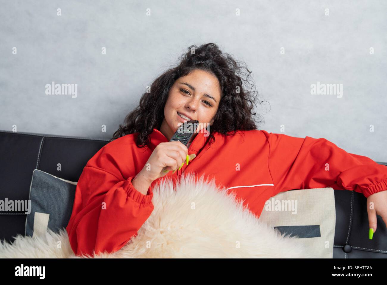 Young woman relaxing on sofa at home, holding a remote control and ...