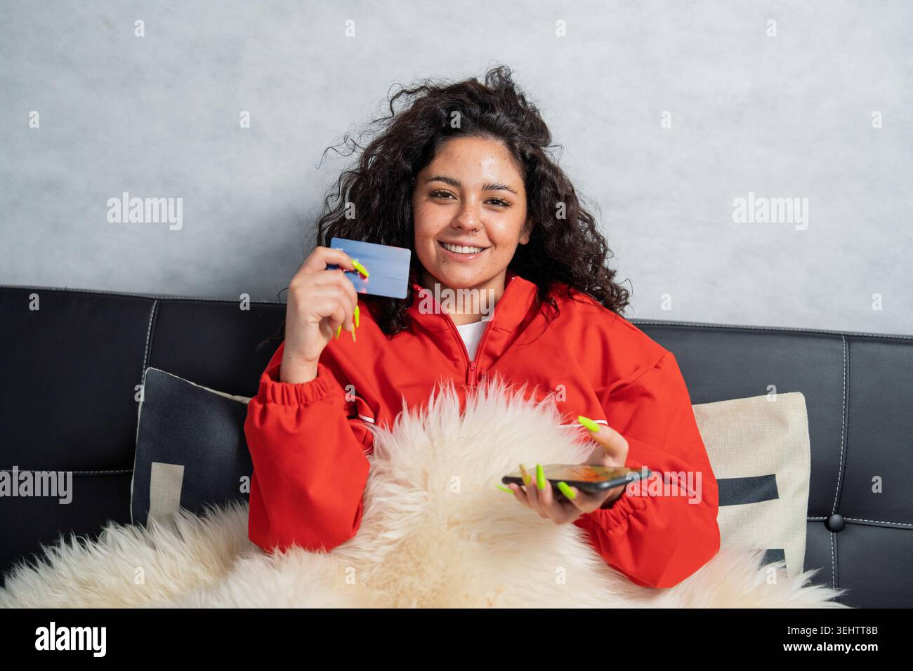 Young woman smiling, holding a credit card and smartphone for online ...
