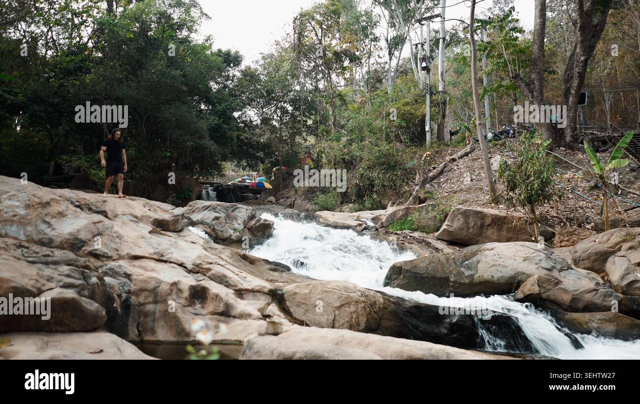 Man standing barefoot on rocks beside a flowing river in a natural ...