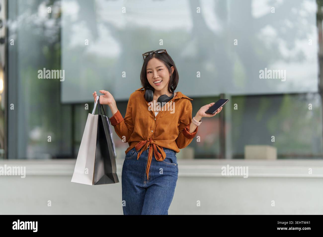 Happy Asian woman with shopping bags and smartphone smiling outdoors ...