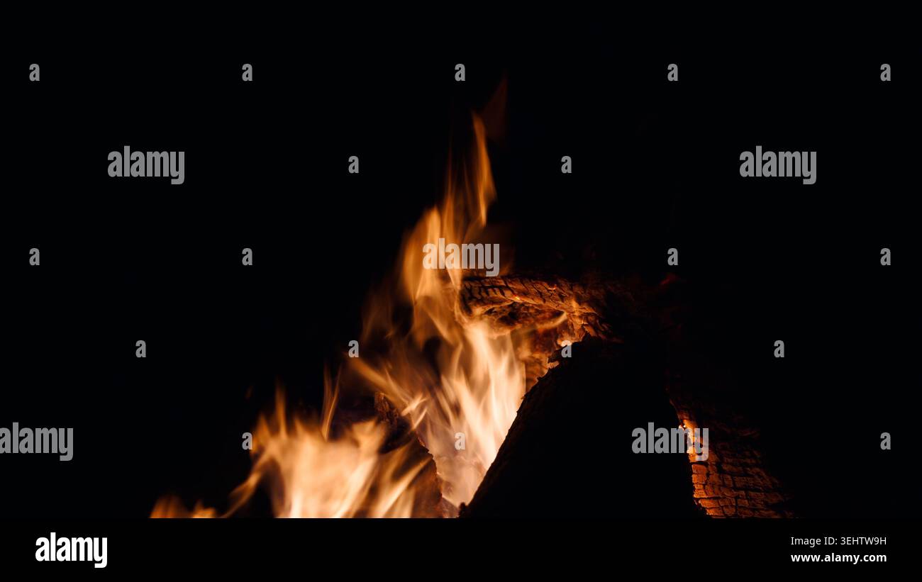 Wood logs burning during a dark night, producing orange flames and ...