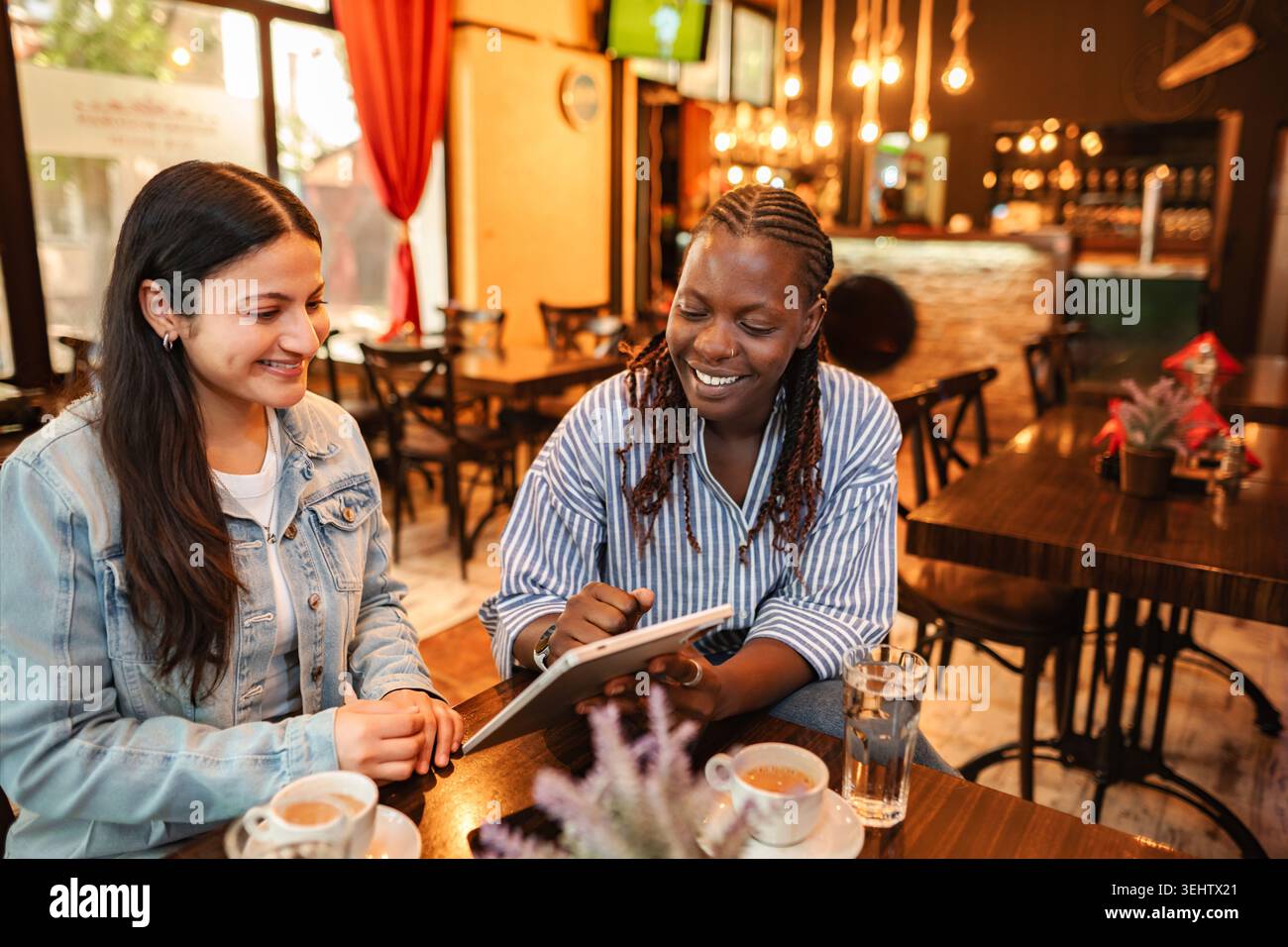 Two diverse women enjoying coffee in a cafe, looking at a digital ...