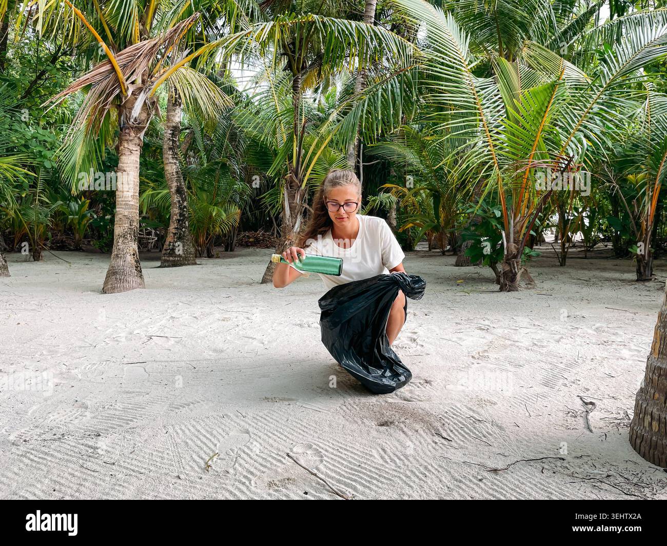 A young female volunteer places a glass bottle in a black bag in a ...
