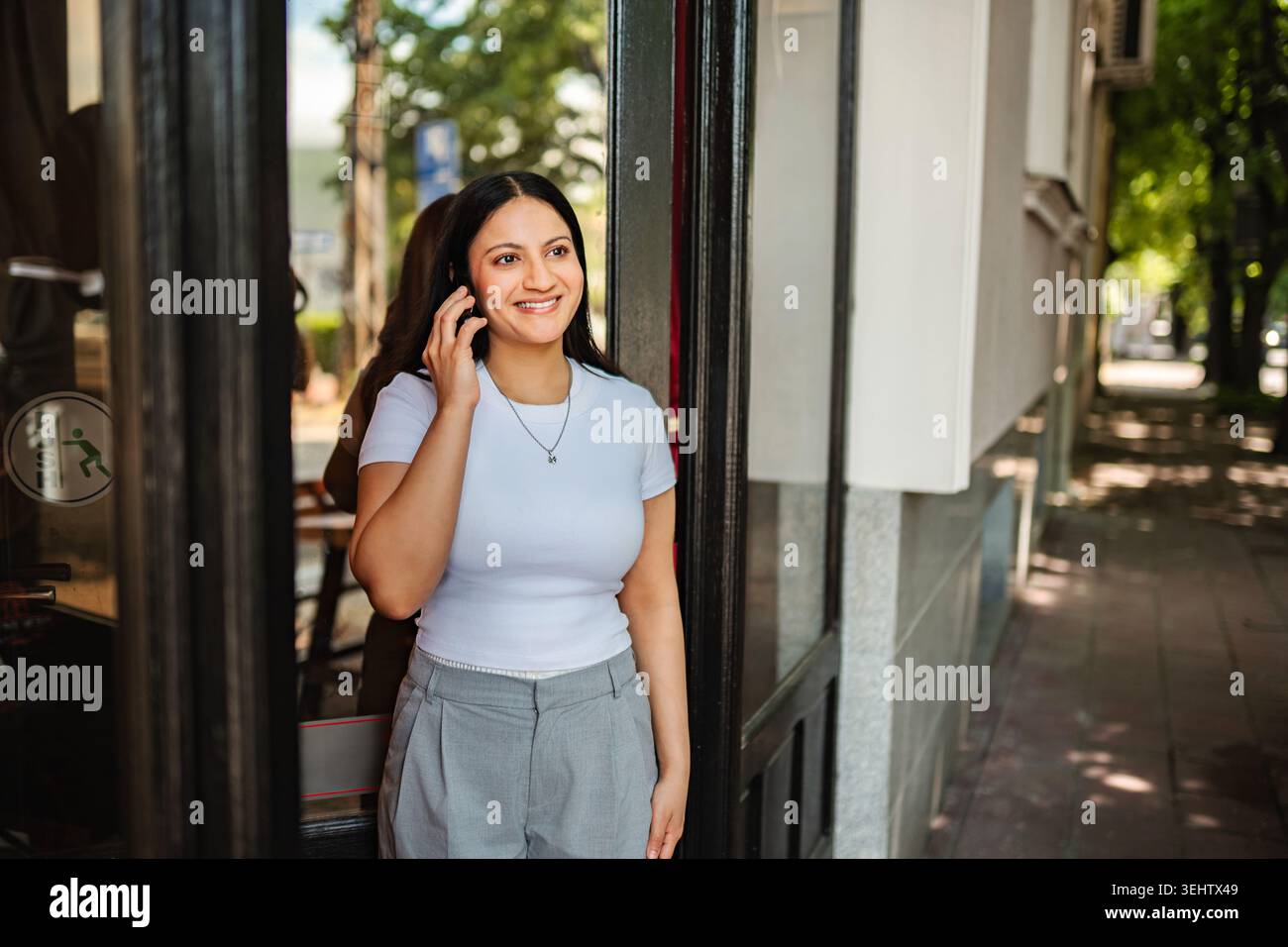 Young woman smiling, communicating on smartphone, standing by a ...