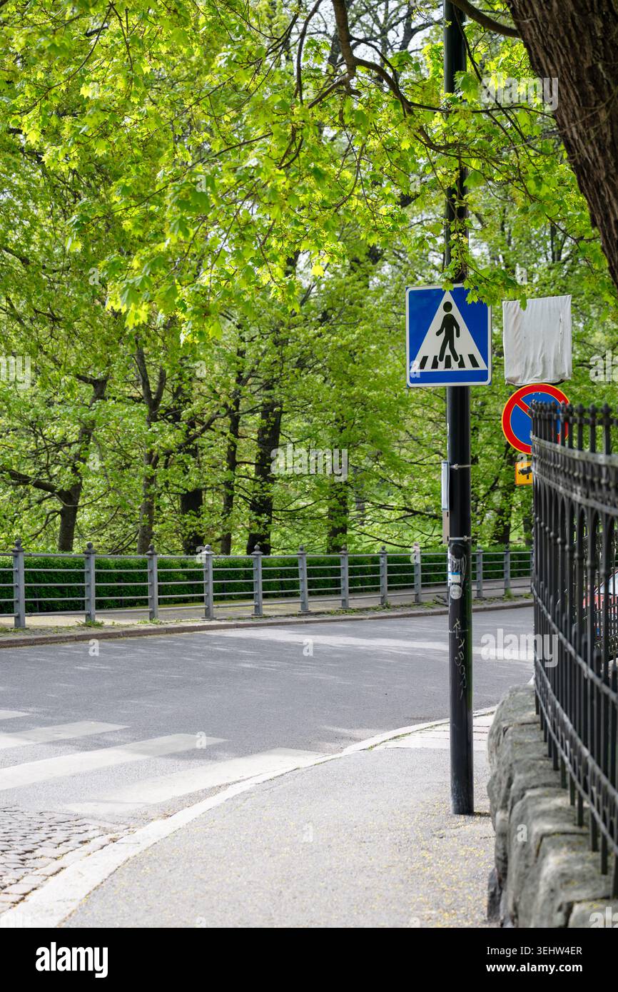 Pedestrian crossing sign on quiet green city street in urban spring ...