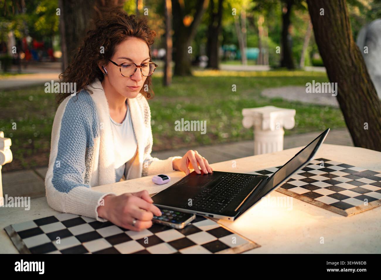 Young adult woman using a laptop and phone at a park table Stock Photo ...