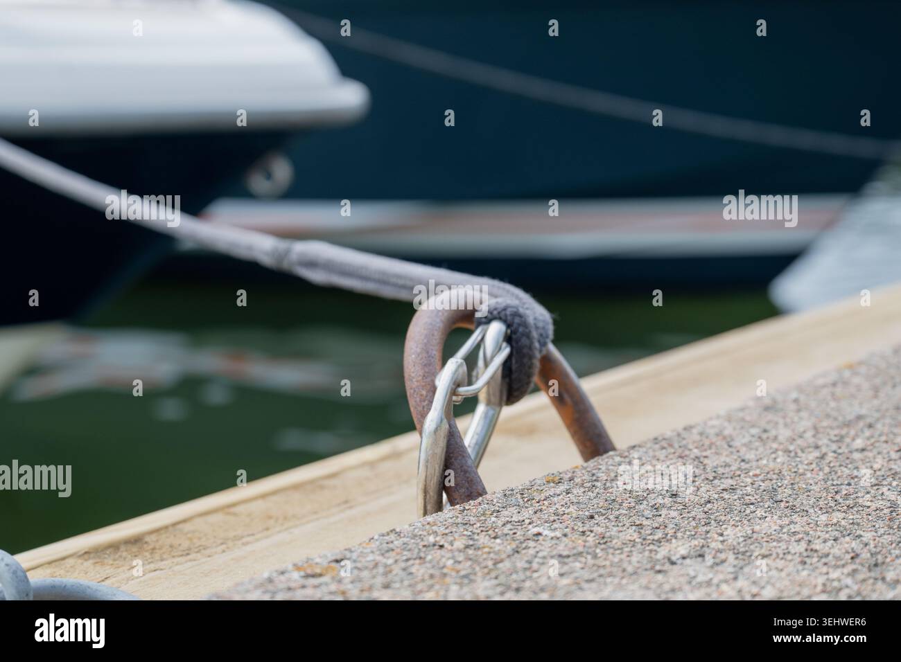 Rusty metal dock ring with mooring rope tied at marina pier near calm ...