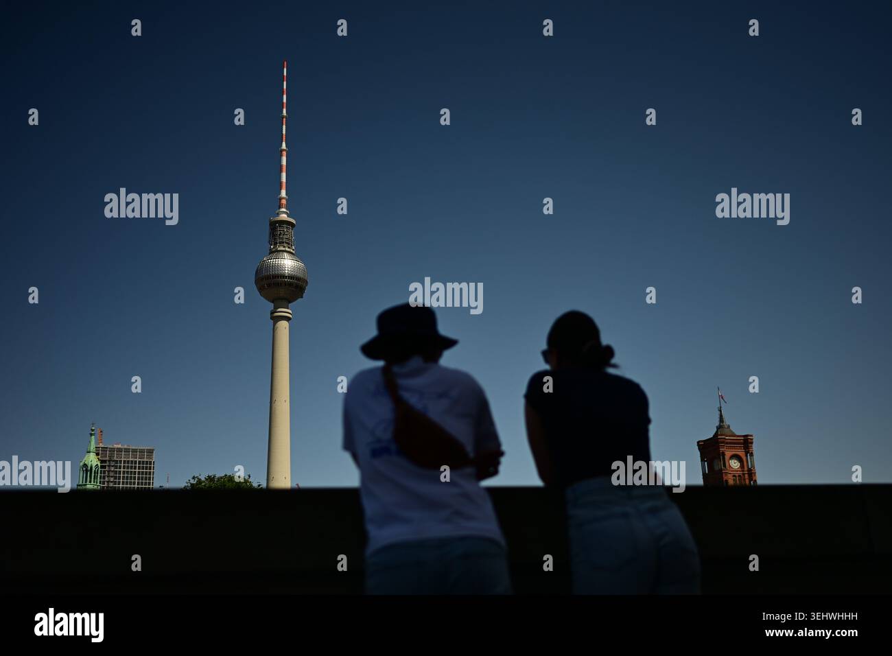26 May 2026, Berlin: Two passers-by stand in front of the television ...