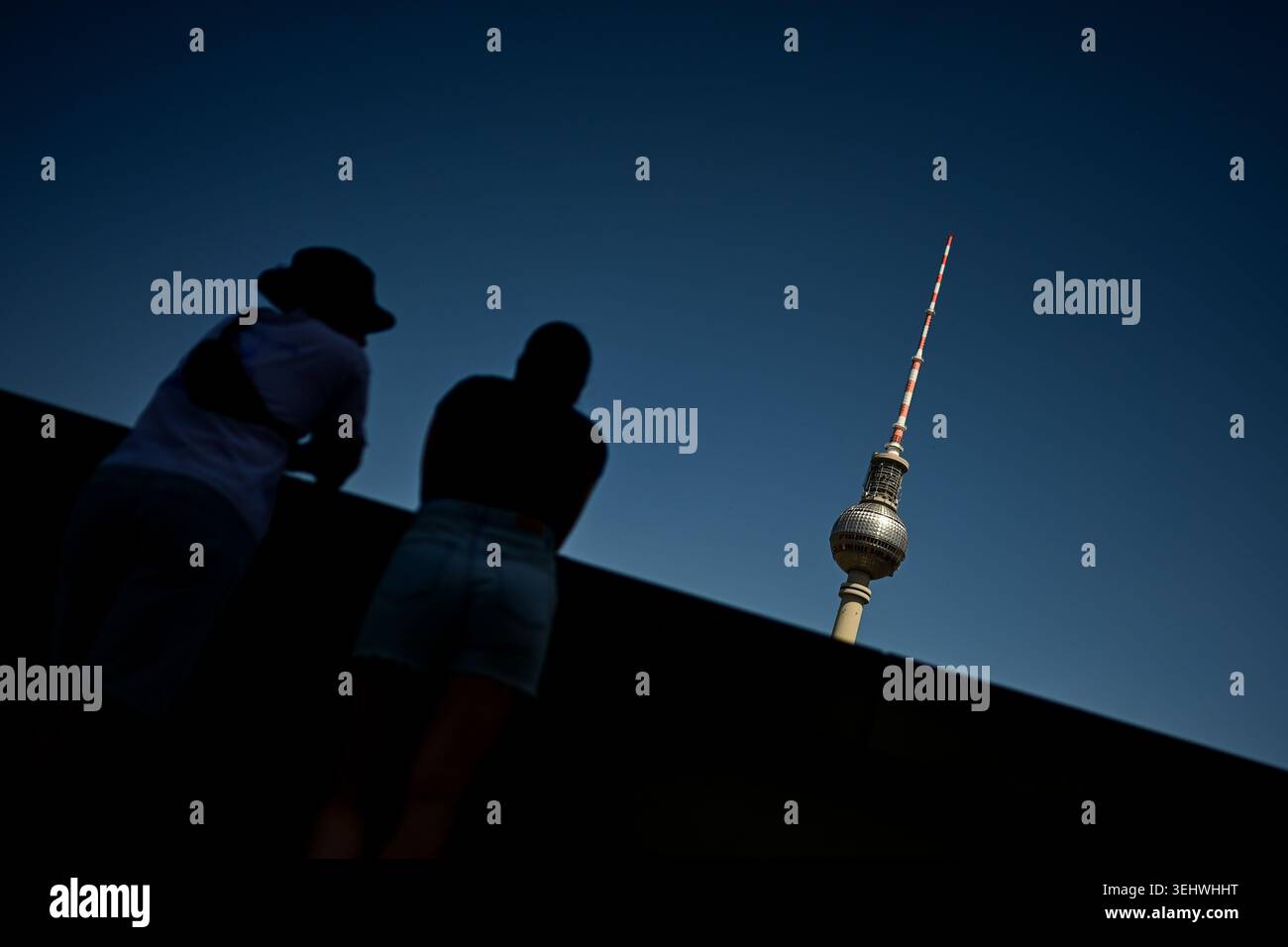26 May 2026, Berlin: Two passers-by stand in front of the television ...